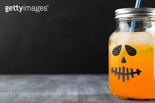 Halloween pumpkin mocktail in glass jar decorated with scary face on ...