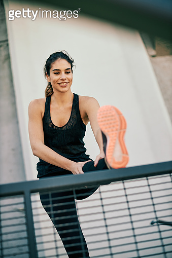 Young smiling fit female runner stretching her leg on railing before ...