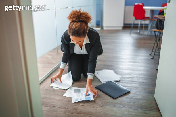 African-American Businesswoman Picking Up Dropped Papers in an Office ...