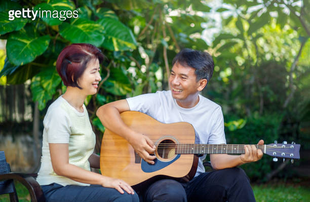 Middle aged couple playing guitar while relax sitting on bench in ...