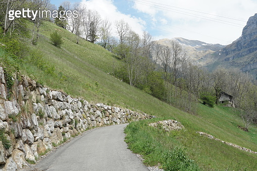 A narrow asphalt road build in the slope of an Alpine hill, reinforced ...