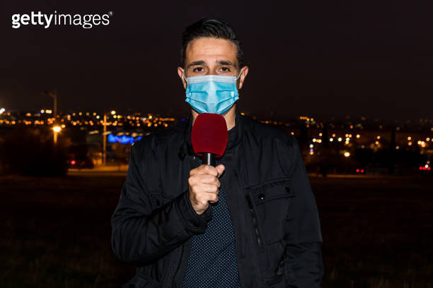 Reporter man wearing blue surgical mask giving the evening news ...