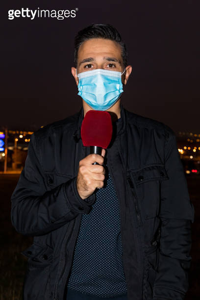 Reporter man wearing blue surgical mask giving the evening news ...