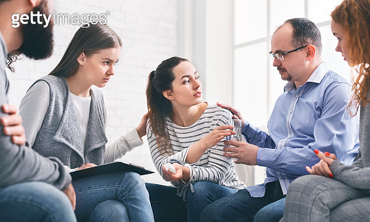 Concerned support group mebers comforting emotional young woman at ...