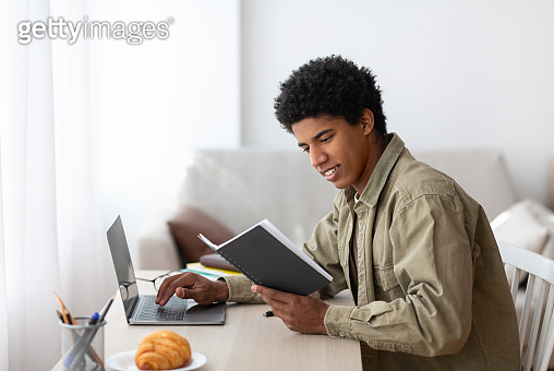 E-learning concept. Handsome black teenager using his notes to make ...