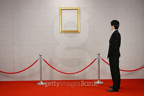 Businessman examining empty picture frame behind velvet rope 이미지 ...