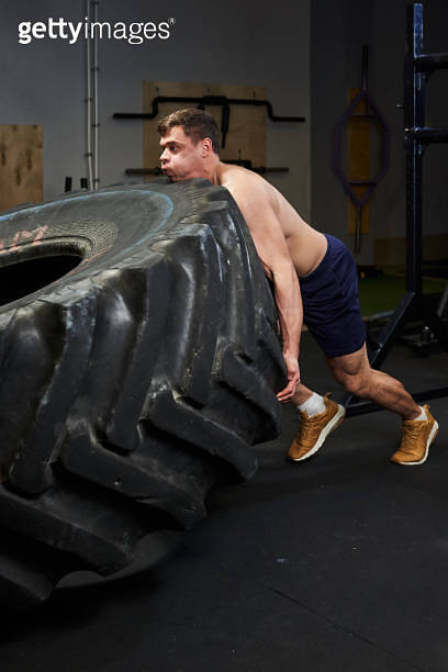 a man training in a gym lifted a huge car tire with great physical ...