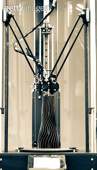 The three-axis 3d printer creates an object in the form of a black vase ...