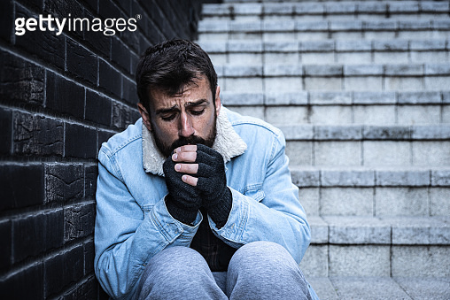 Young sick depressed homeless hobo man with mental issues sitting on ...