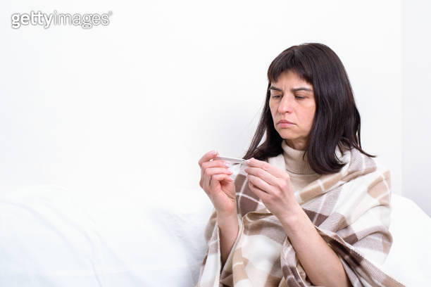 Sick day at home. Sick woman covered with a blanket holds a thermometer ...