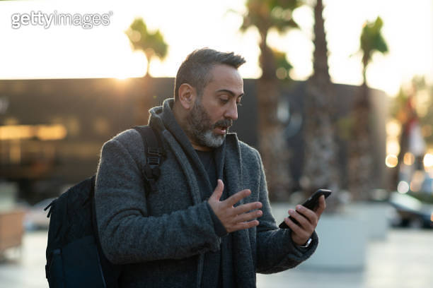 Portrait of an upset man looking at his mobile phone (1312189006) - 게티이미지뱅크