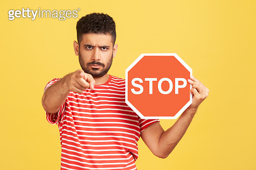 Strict angry man with beard in striped t-shirt holding stop sign and ...