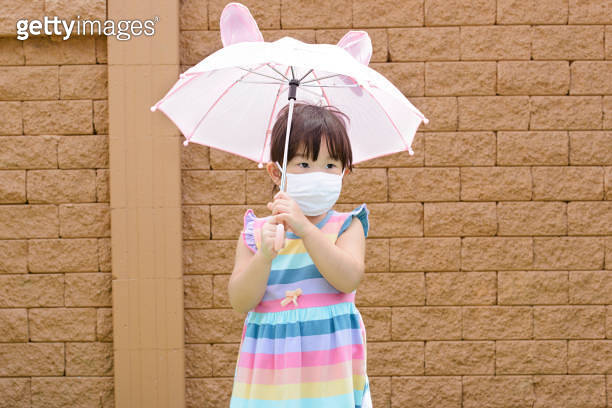 Little Asian girl holding an umbrella and wearing face mask protection ...