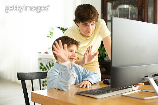 Smiling boy and teenager chatting online and waving at the computer ...