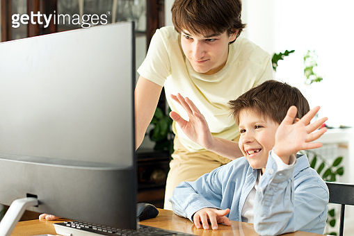 Smiling boy and teenager chatting online and waving at the computer ...