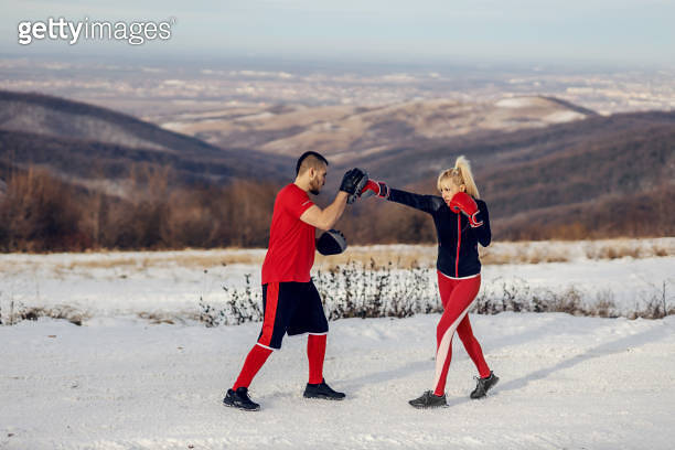 Sportswoman sparring with boxing gloves in nature at snowy winter day ...