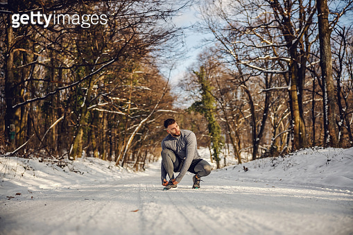 Sportsman crouching and tying shoelace in nature at sunny snowy winter ...