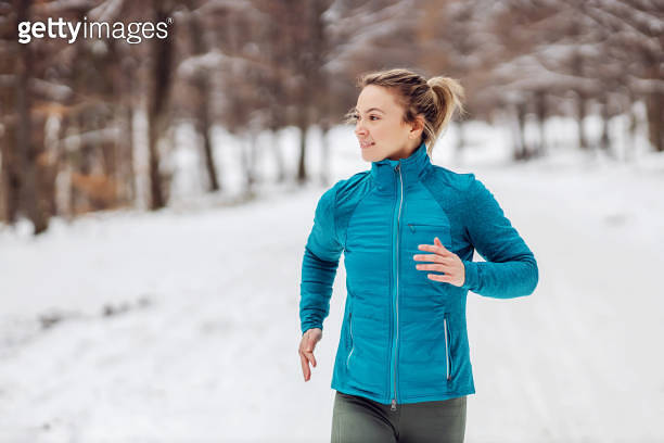Fit sportswoman jogging in nature on a snowy weather. Cold weather ...
