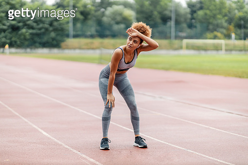 A panting, tired runner stands in the stadium and taking a break after running on a rainy autumn ...