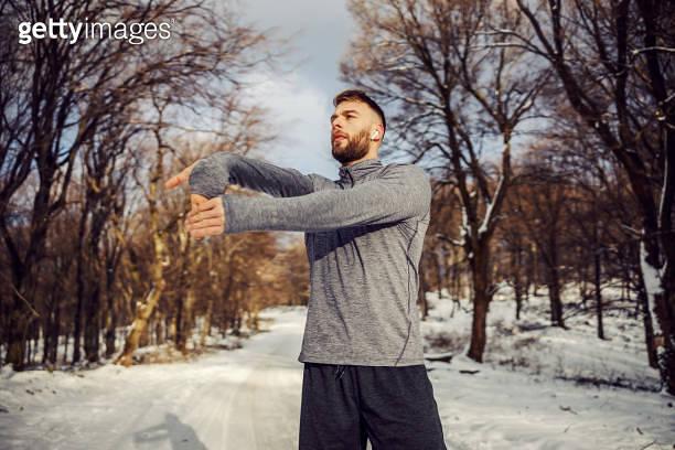 Sportsman standing in nature and doing warm up exercises at snowy ...