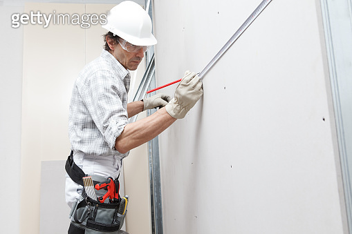 Side view of male drywall worker or plasterer taking measures on ...
