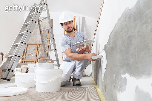man plasterer construction worker at work, takes plaster from bucket ...