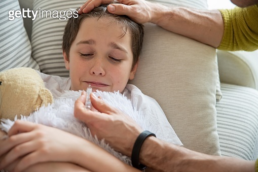 A sad crying child is lying sick on the couch. Father measures the ...