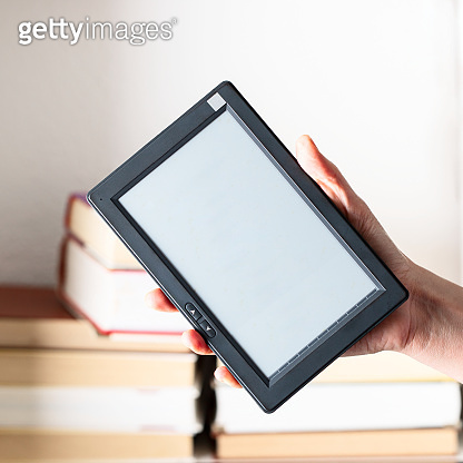 Hand holding e-book reader device against the book closet with many ...