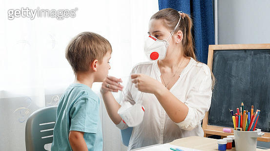 Young woman putting protective mask on little boy before studying and ...