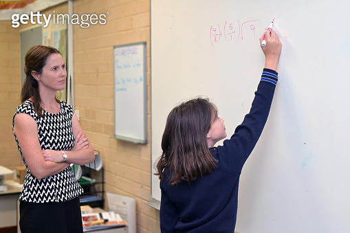 Female student solving a math question on a whiteboard in school ...