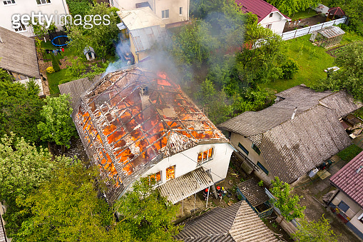 Aerial view of a house on fire with orange flames and white thick smoke ...