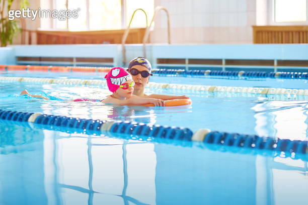 Portrait of mother or coach learning to swim with flutter board little ...