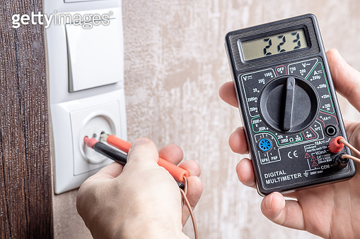 handyman electrician measuring wall outlet voltage at living room ...