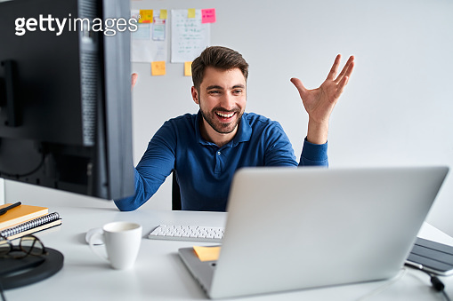 Excited young man cheering while working at office on computer ...