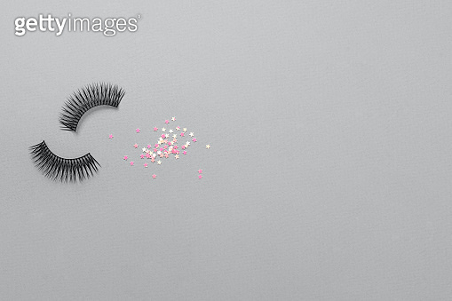 Fake eyelashes and sparkling confetti on trendy gray color background ...