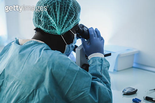 African medical worker in hazmat suit working with microscope inside ...
