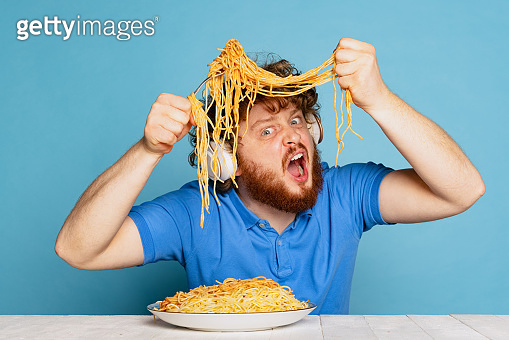 Crazy young hairy red-bearded man tasting large portion of noodles ...