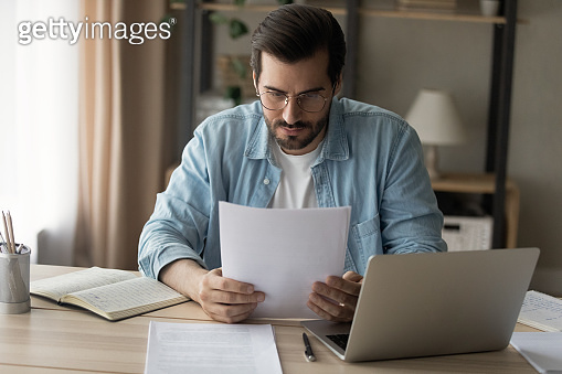 Concentrated young man in glasses looking through paper correspondence ...