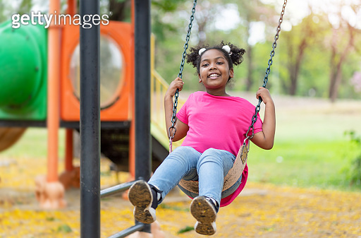Cute African American little girl playing on swing. Smiling child ...