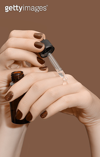 Female hands holding essential oil dropper on brown background. Female ...