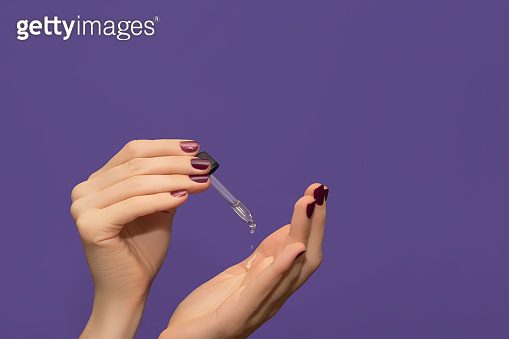 Female hands holding essential oil dropper on purple background. Female ...