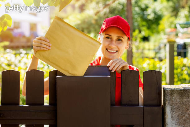 smiling postman mail carrier inserting envelope into mailbox ...