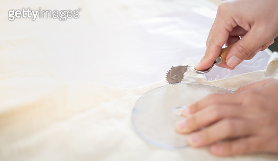 Closeup of tailors table with female hands tracing fabric with curve ...