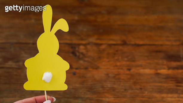 Yellow rabbit made of paper on a toothbrush. Hand holds Easter baking ...