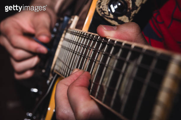 Person plucking the strings on the frets of an electric guitar ...