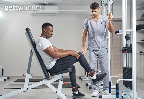 Focused male patient doing strength training exercise supervised by ...