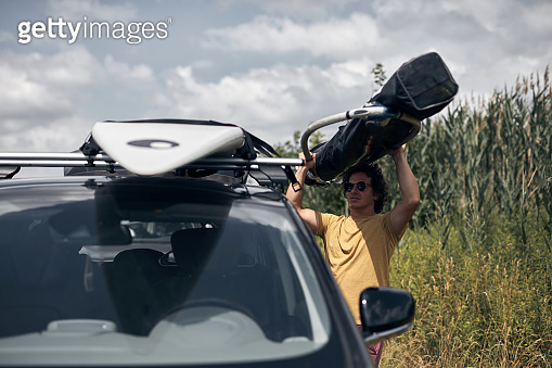Windsurfer and camper packing and unpacking from a car's roof rack in ...