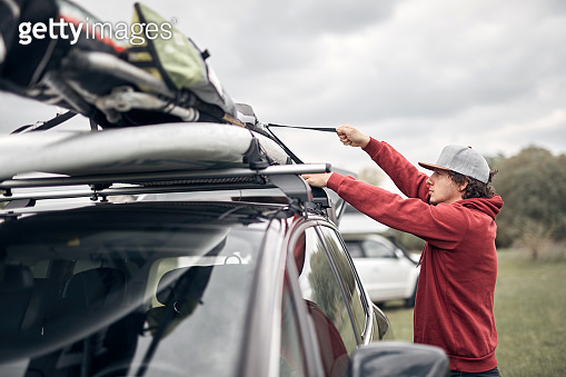Windsurfer and camper packing and unpacking from a car's roof rack in ...