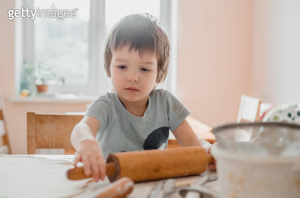 Cute little boy using rolling pin to prepare the dough for cookies in ...