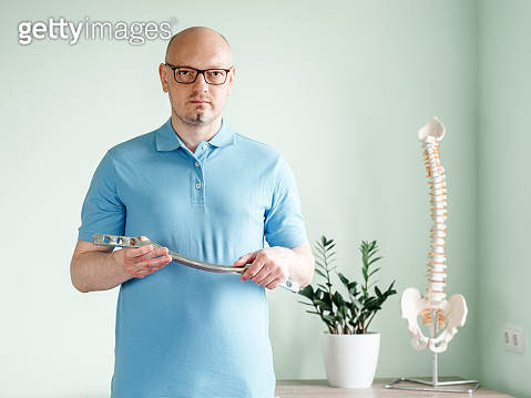 A male osteopath practitioner holding a stainless IASTM treatment tool ...